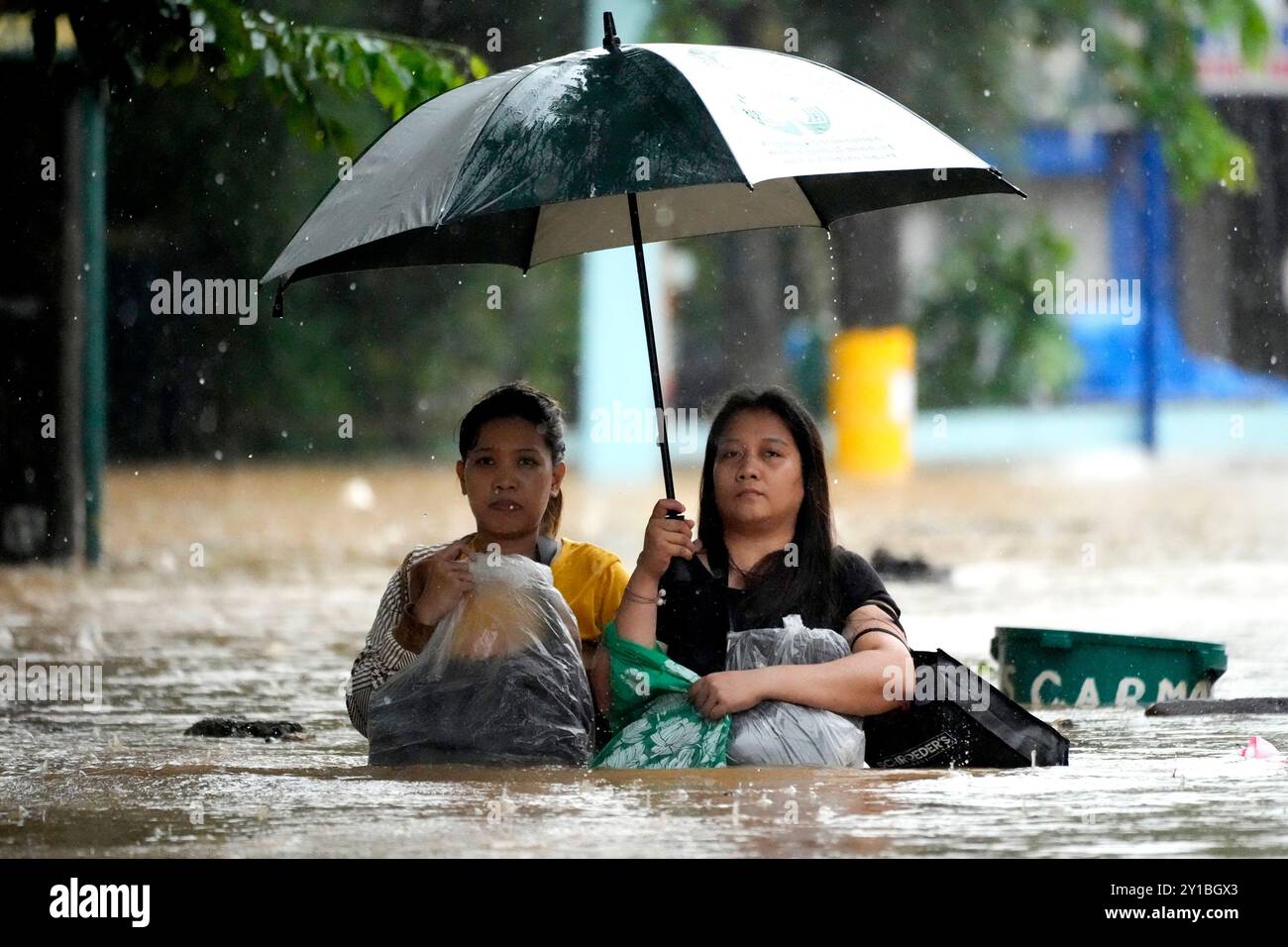 Residents protect their belongings as they negotiate a flooded street ...
