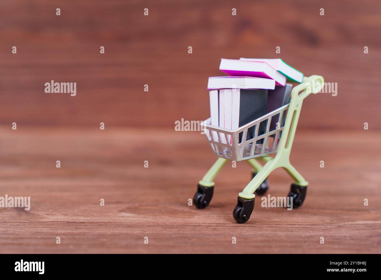Mini shopping cart with books positioned on wooden texture background ...
