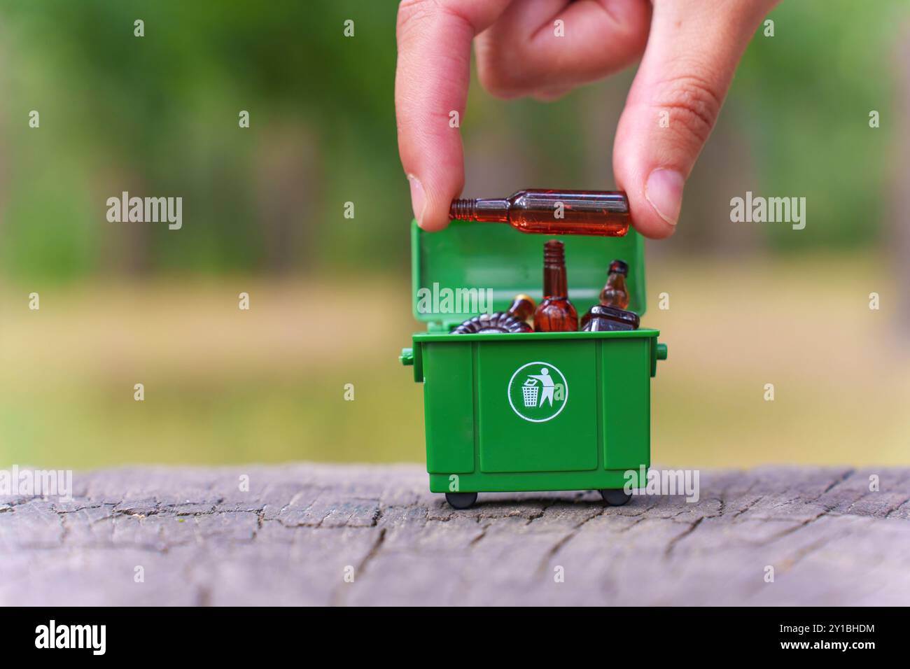 Hand placing a tiny glass bottle into a miniature green trash bin ...