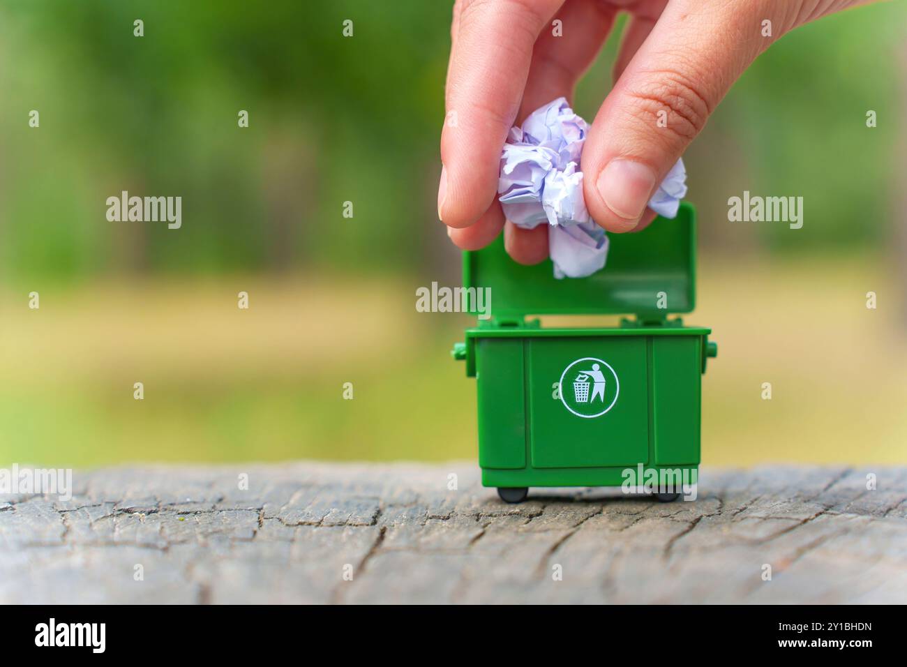 Hand dropping crumpled paper into a miniature green trash bin in a ...
