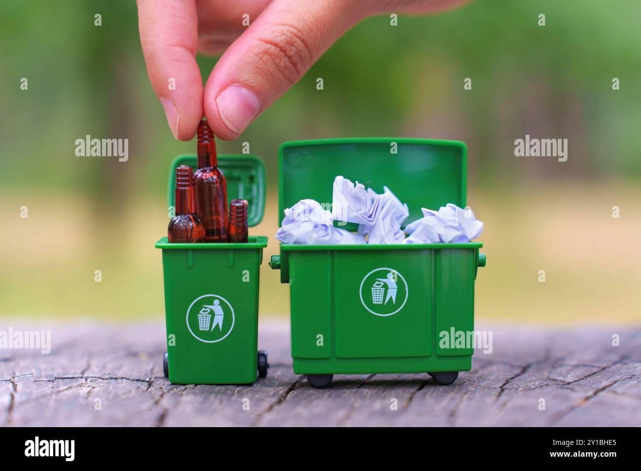 Hand dropping glass bottles into a green miniature bin, representing environmentally friendly ...