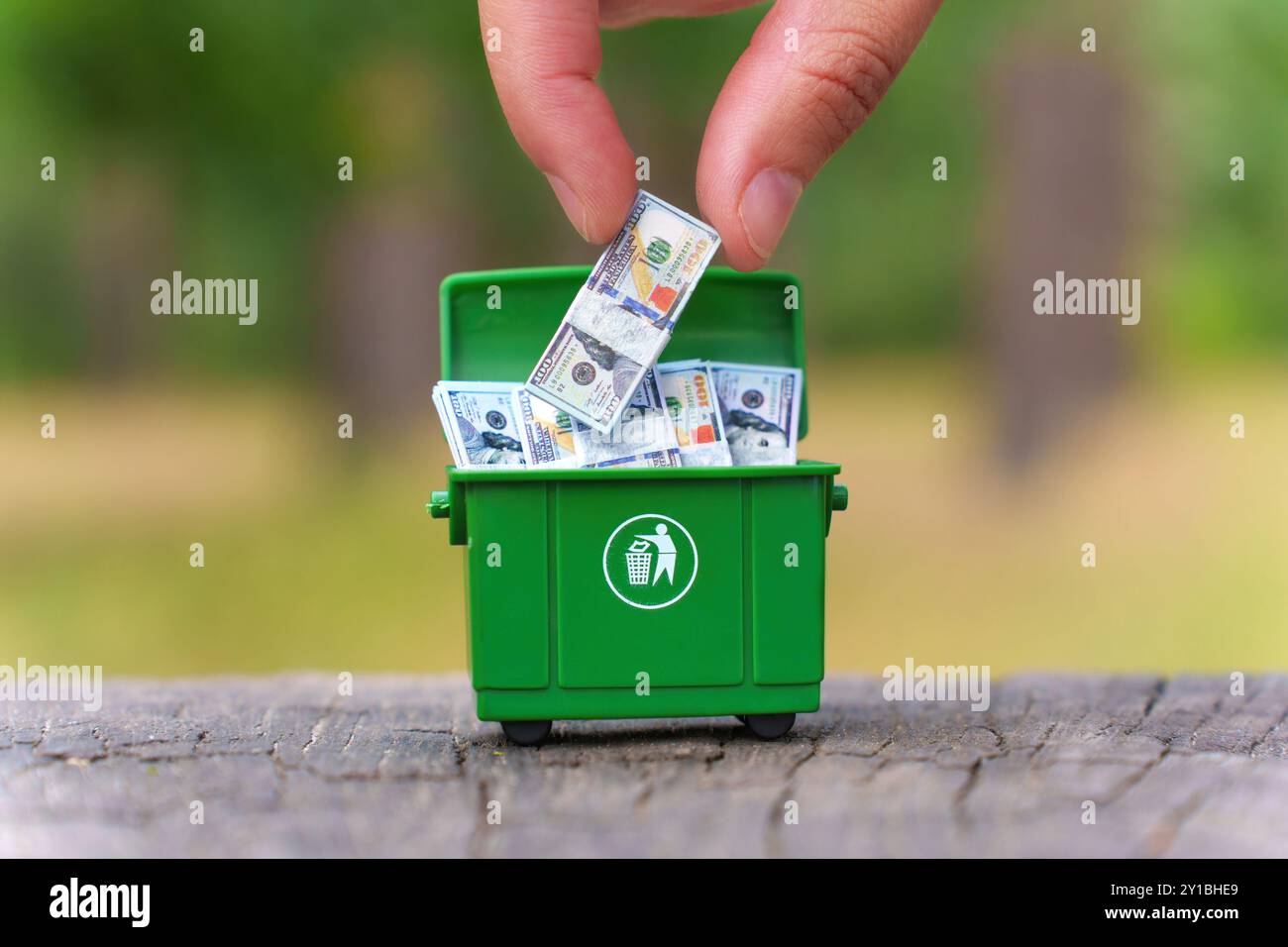 Close-up of a hand dropping cash stack into a trash bin, representing ...