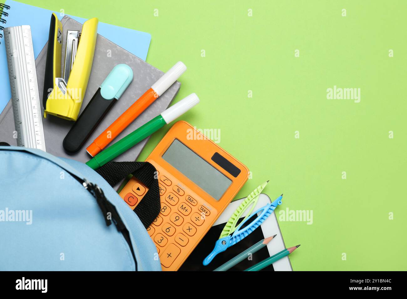 Light blue school backpack with stationery on green background, top ...