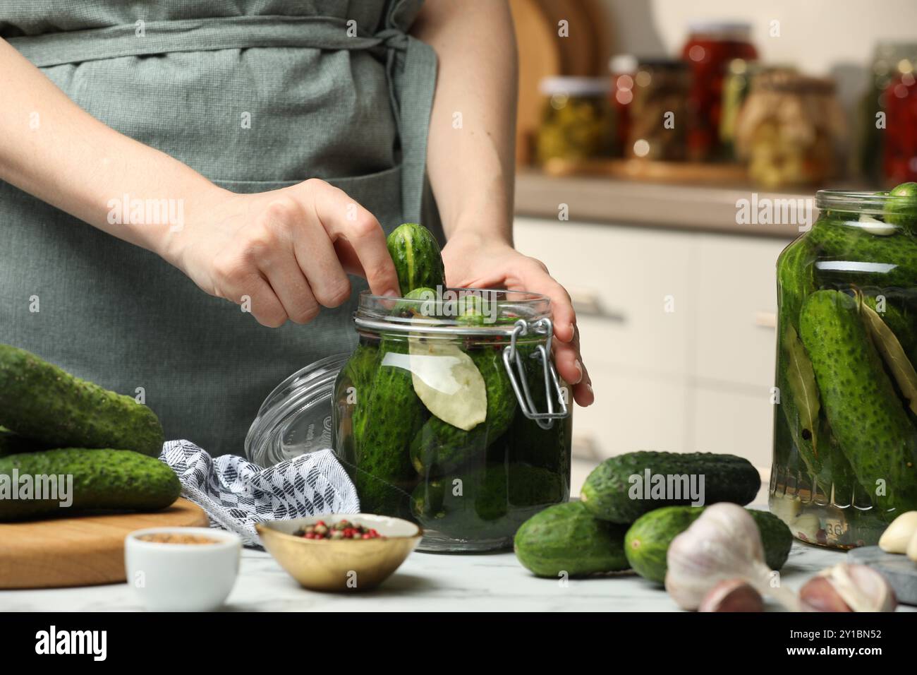 Making pickles. Woman putting cucumber into glass jar at white marble ...