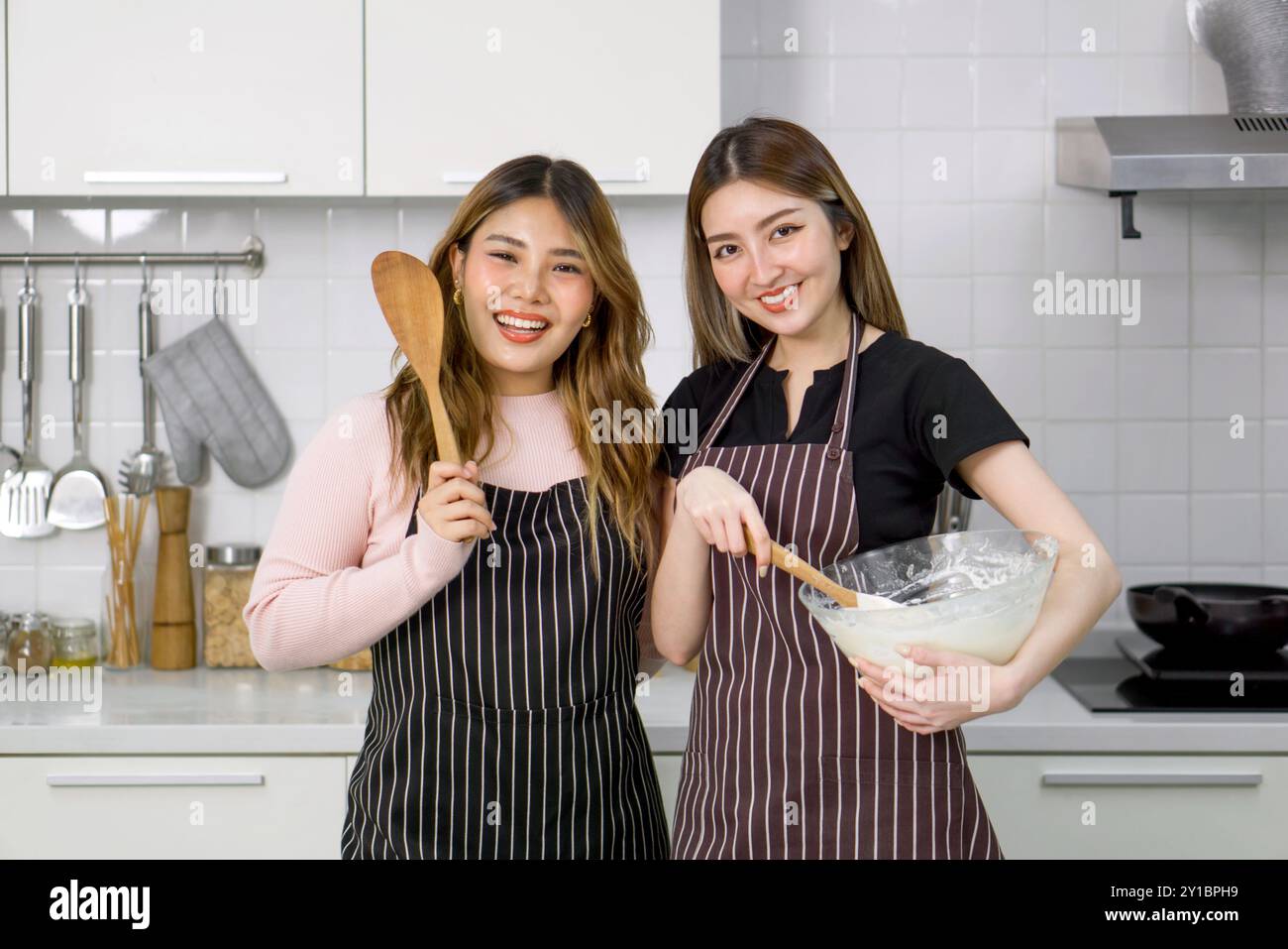 Two women are having fun baking together. They are wearing apron and ...