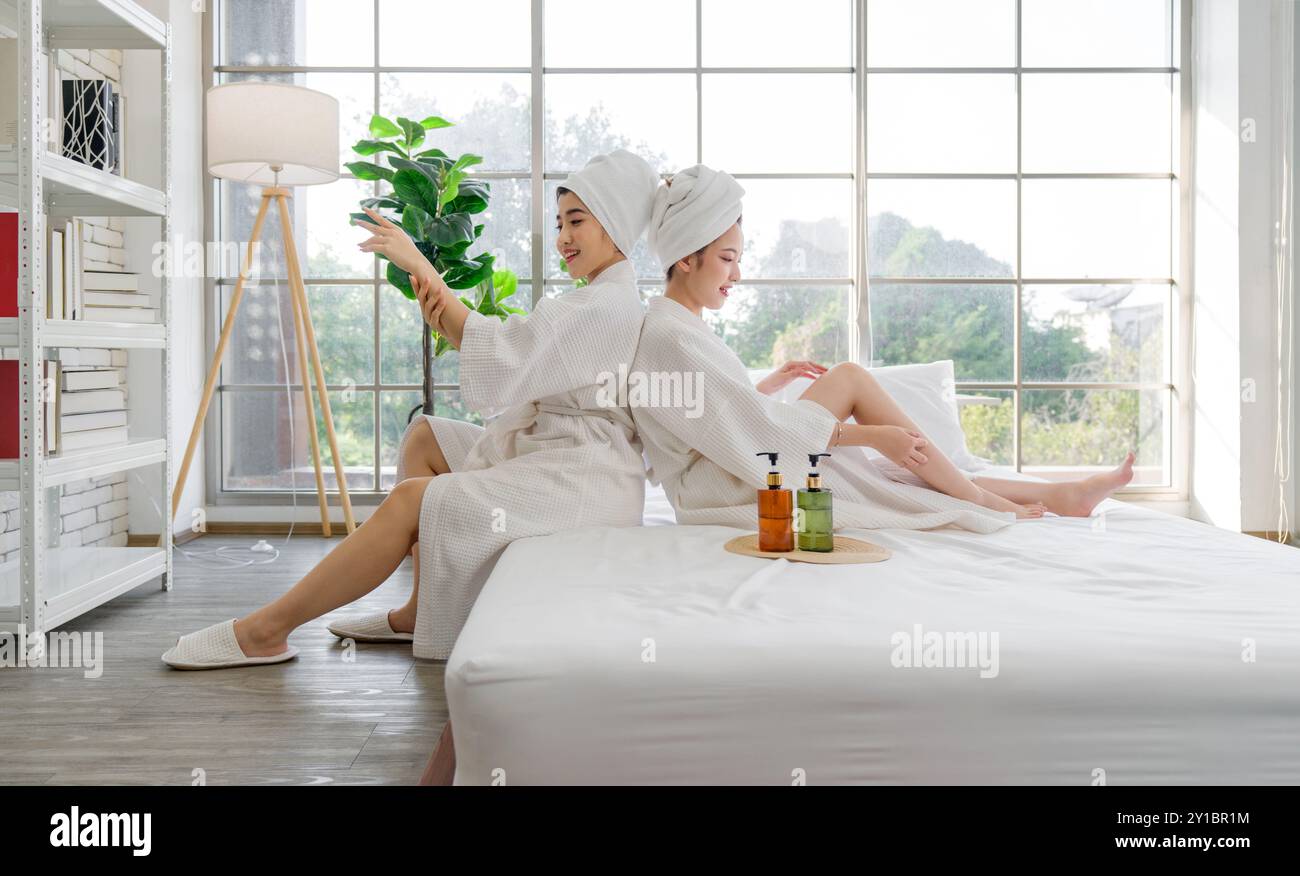Two asian women are sitting relax on a bed in white robe and towel ...