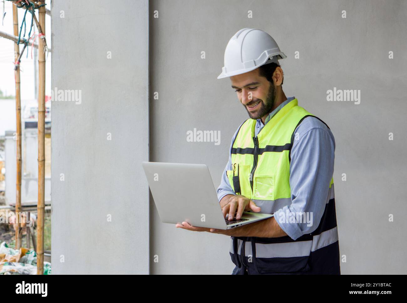 Young engineer in hardhat and safety vest typing on laptop computer ...