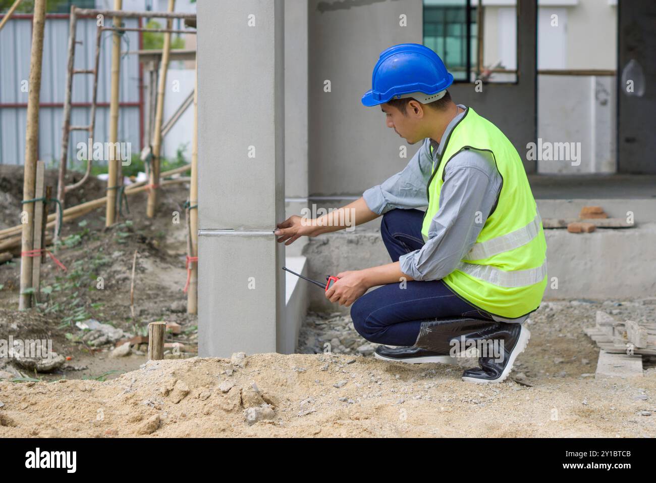 Young engineer in a construction helmet and safety vest checking house structure while holding ...