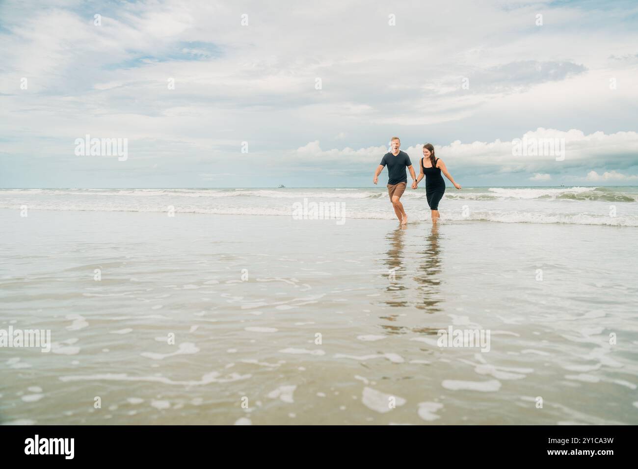 Couple running playfully along the shoreline, holding hands Stock Photo ...