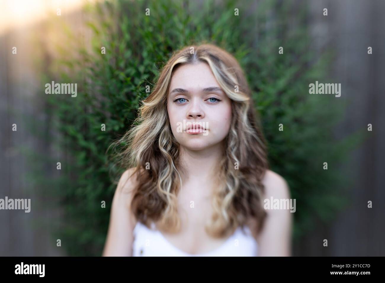 Woman with soft expression, blue eyes, in golden light and greenery ...