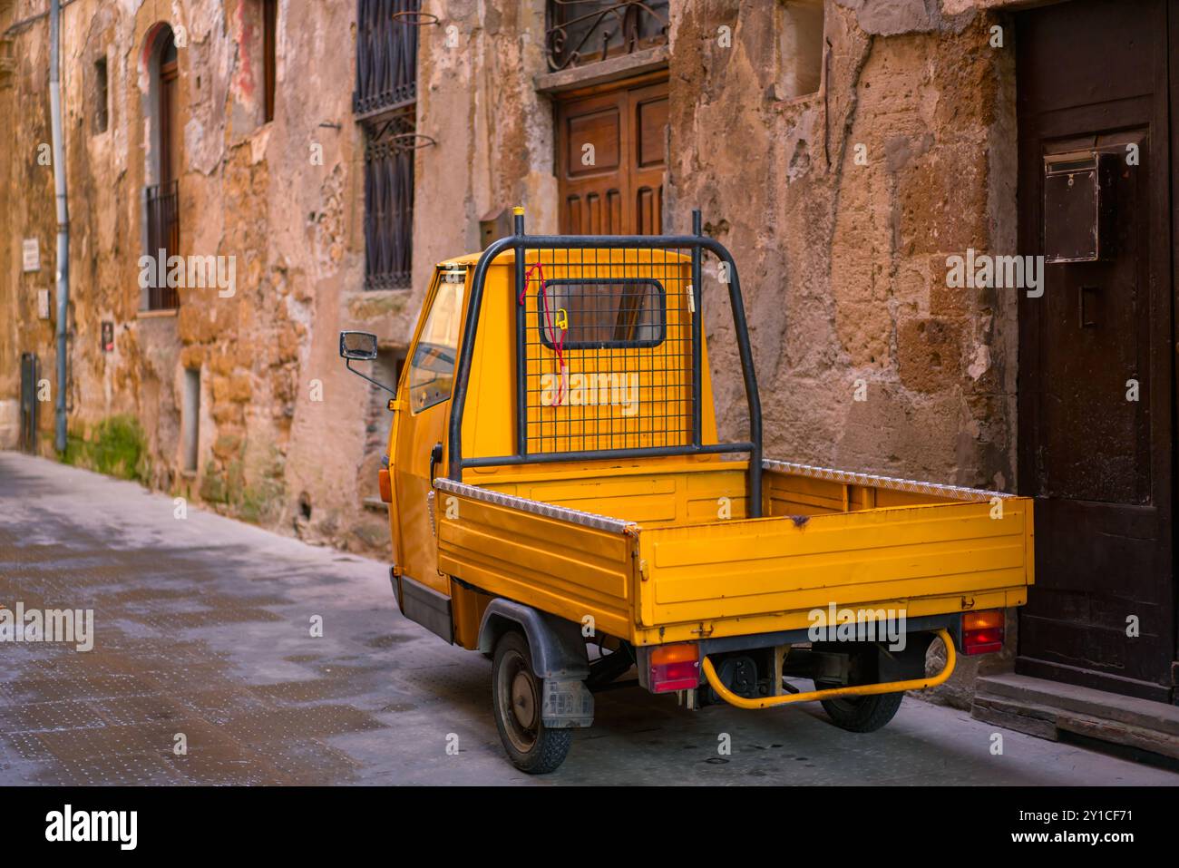 Iconic yellow Piaggio Ape three wheeler on an antique street of Italy ...