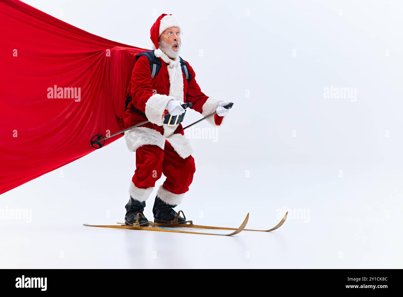 Santa Claus skiing, pulling large red cape behind him, gripping poles ...
