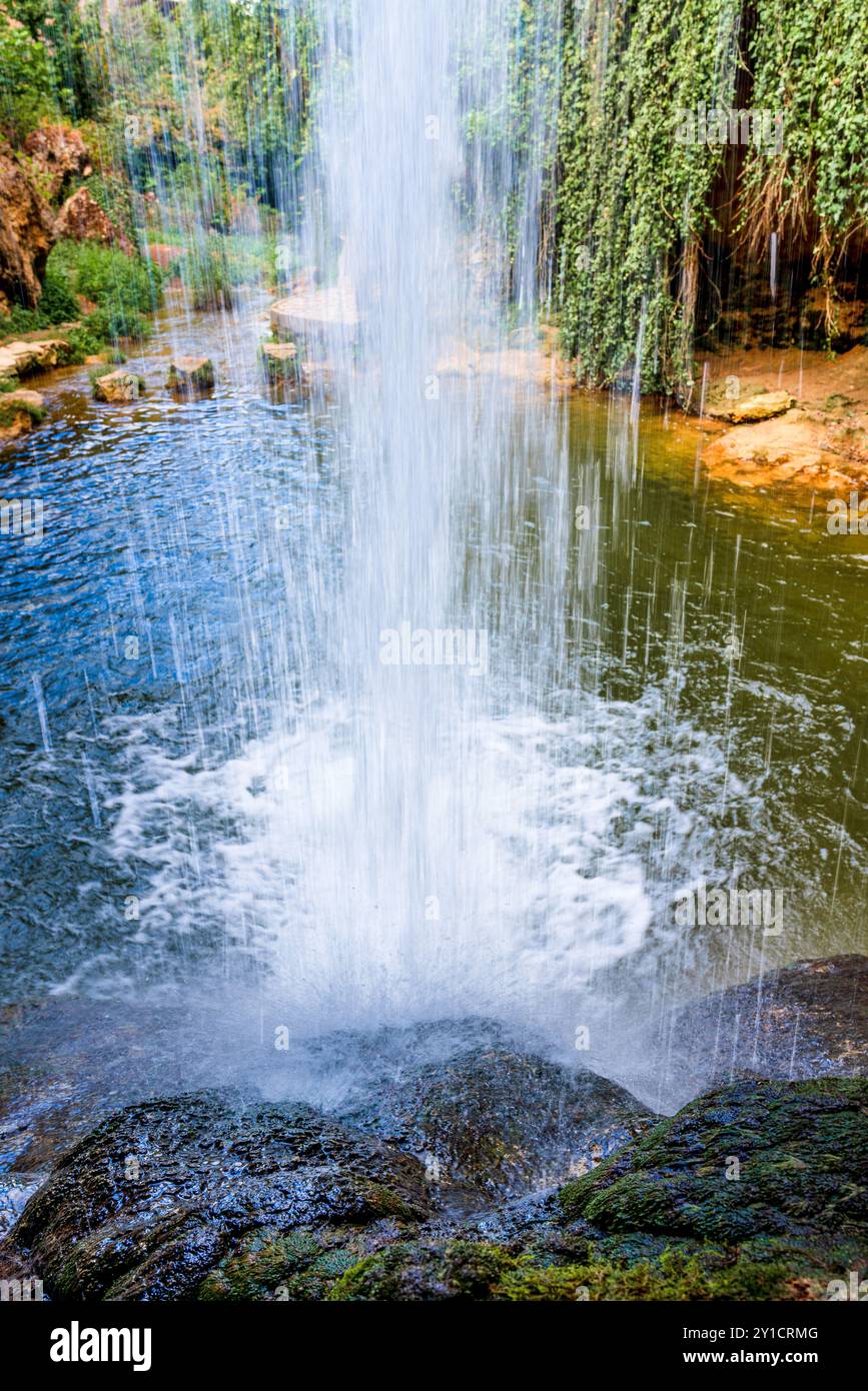 A serene waterfall cascades over rocks into a tranquil pool surrounded ...