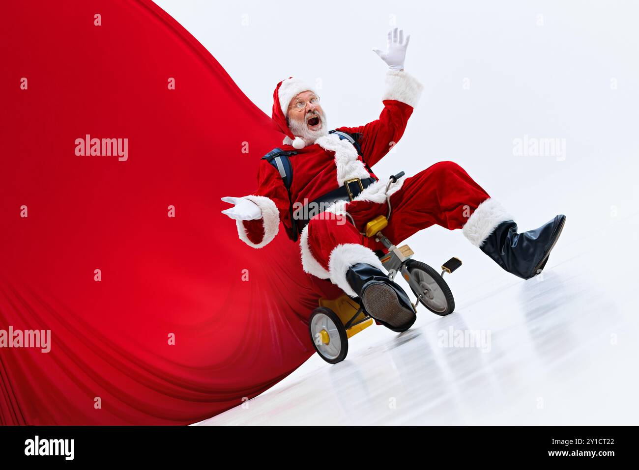 Santa Claus on small tricycle, holding red bag of gifts behind him ...