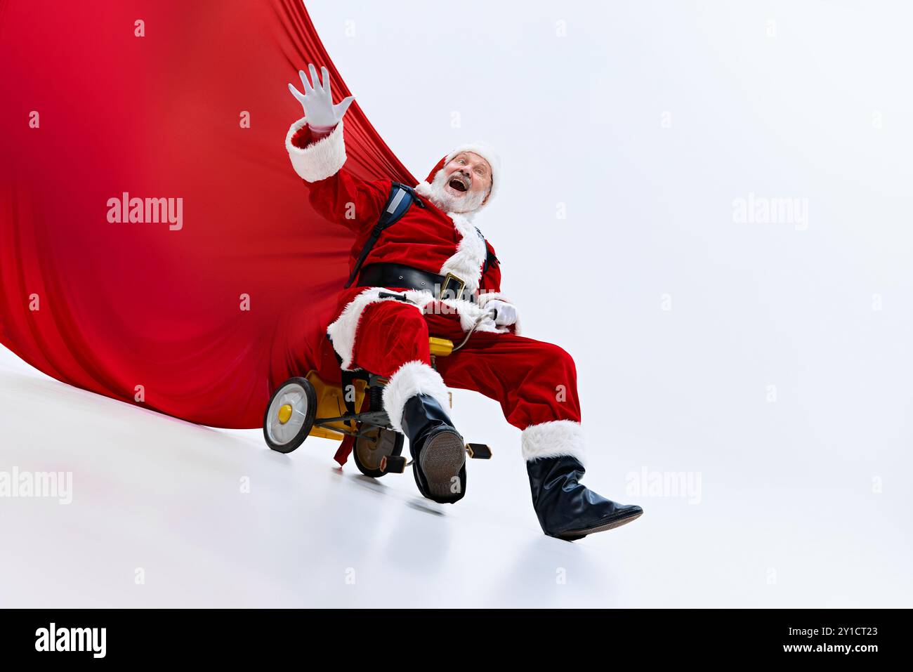 Santa Claus on small tricycle, holding red bag of gifts behind him ...