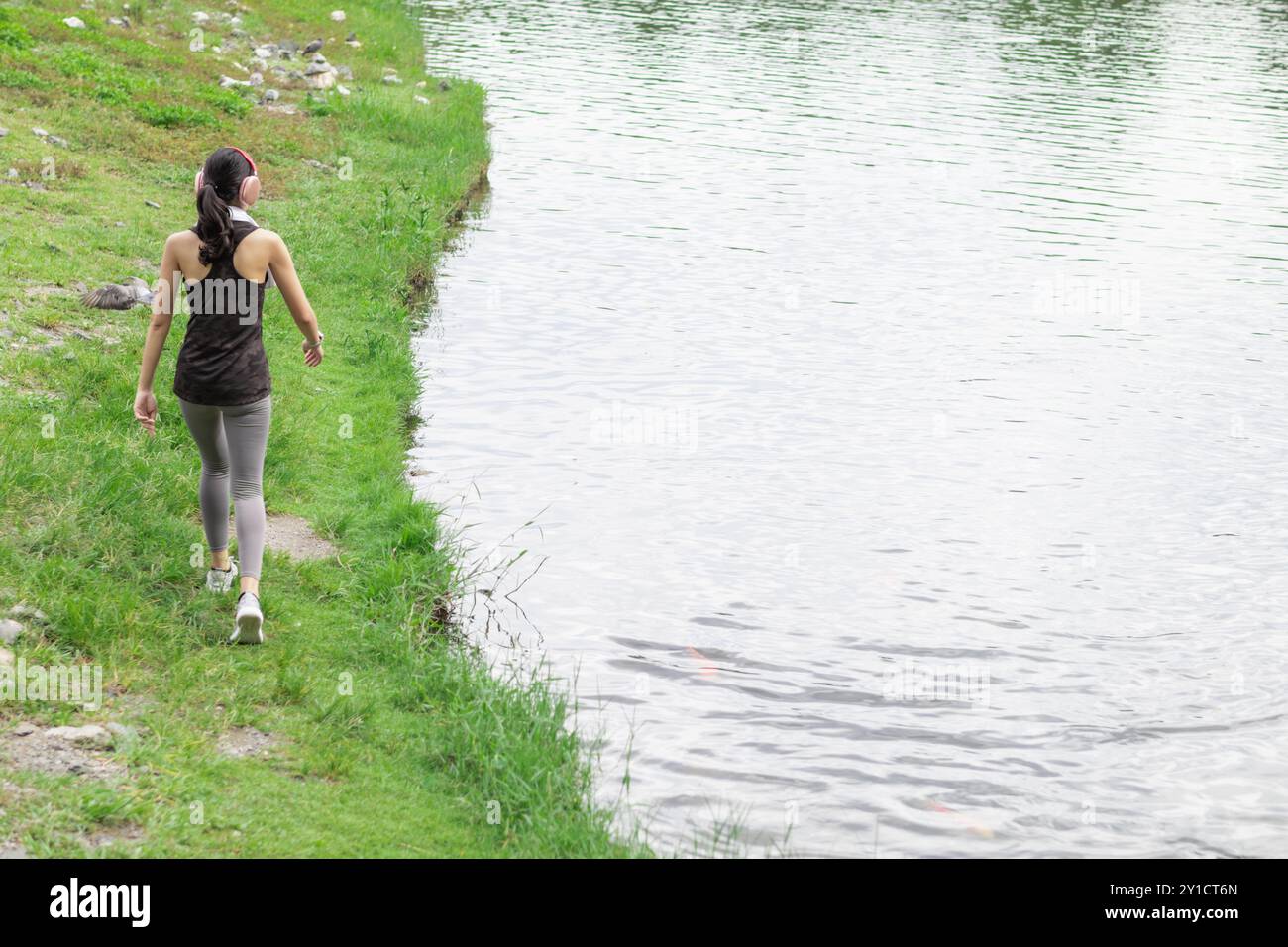 Asian woman wearing sports bra walking along path by reservoir in ...