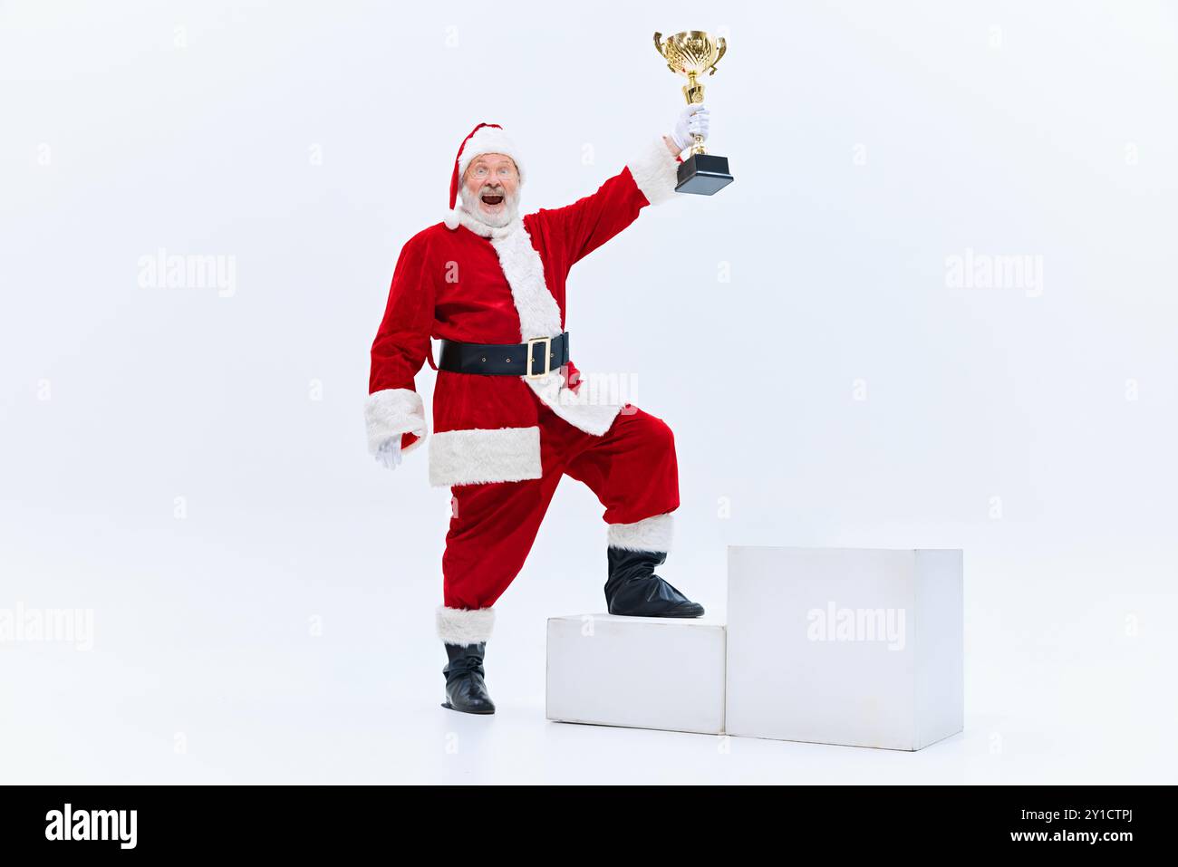 Santa proudly holds a trophy, standing with one foot on podium, showing ...