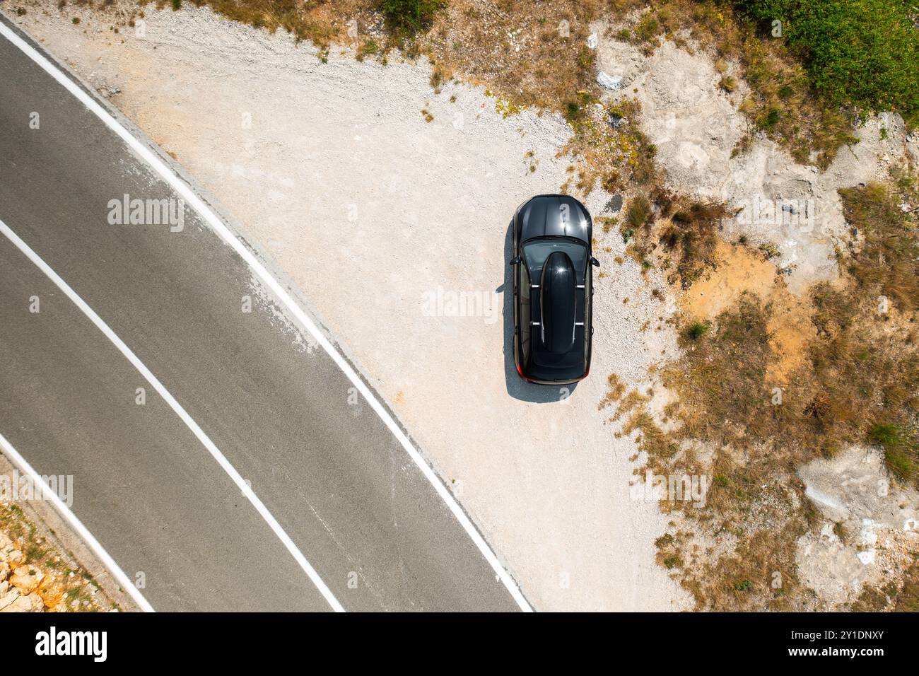 Top view of black car with a roof box, parked beside a coastal road on ...