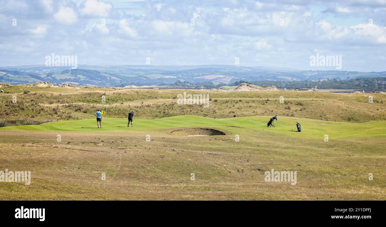 Pair of golfers on the green in front of bunker at Royal North Devon Golf Course with beautiful ...