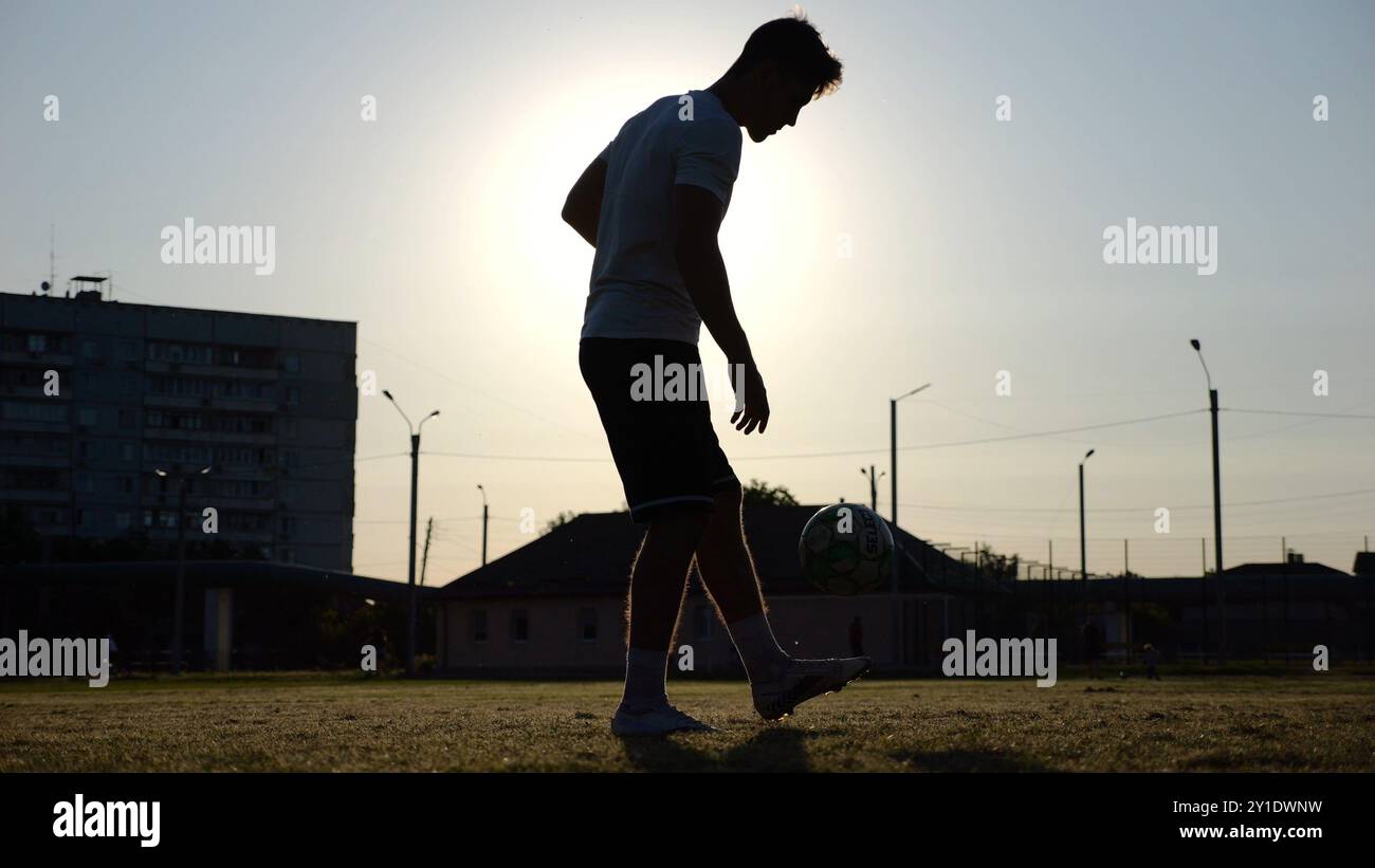 Professional footballer juggling soccer ball on stadium at sunset ...