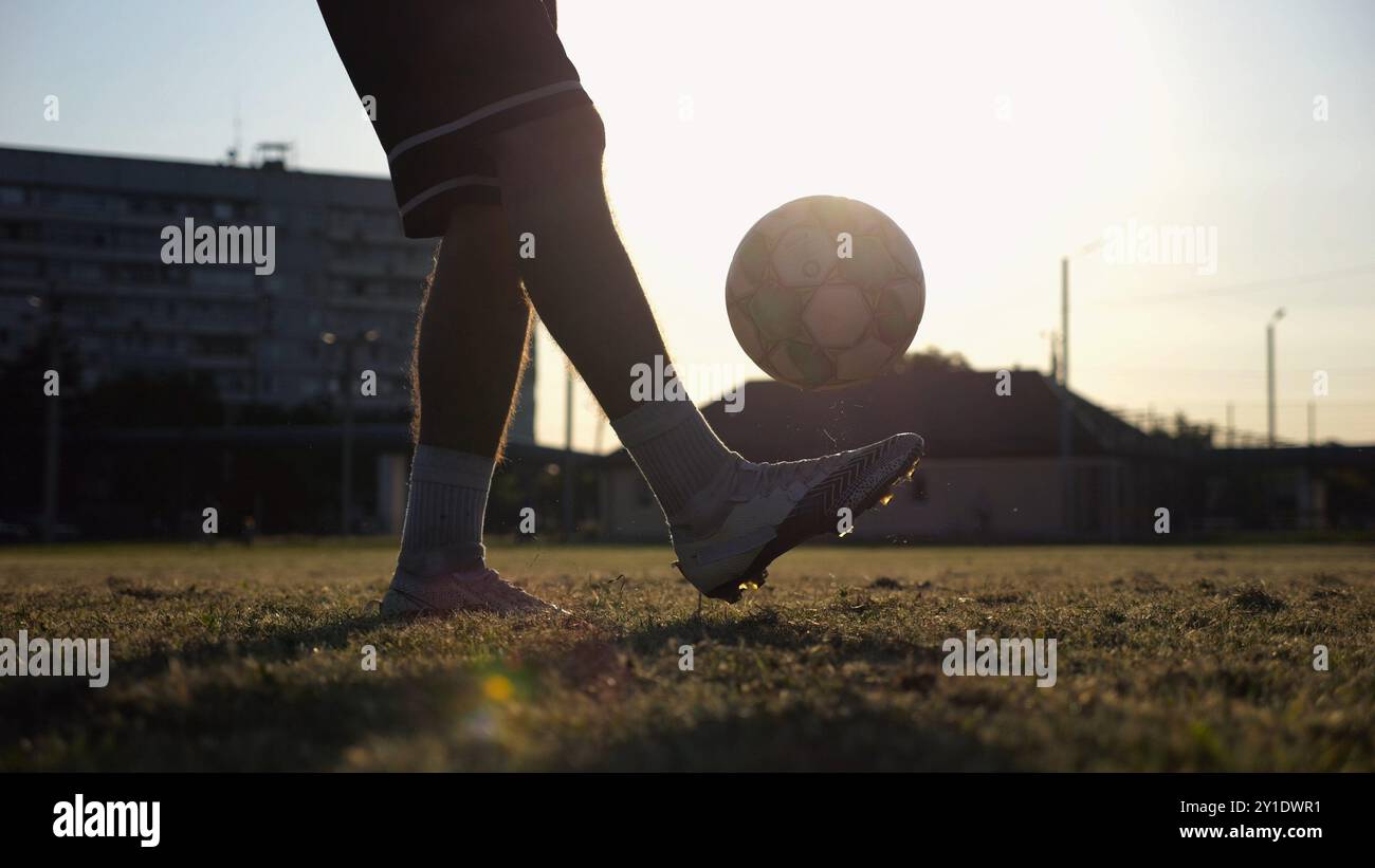 Legs of young man kicking ball at green field. Male feet of ...