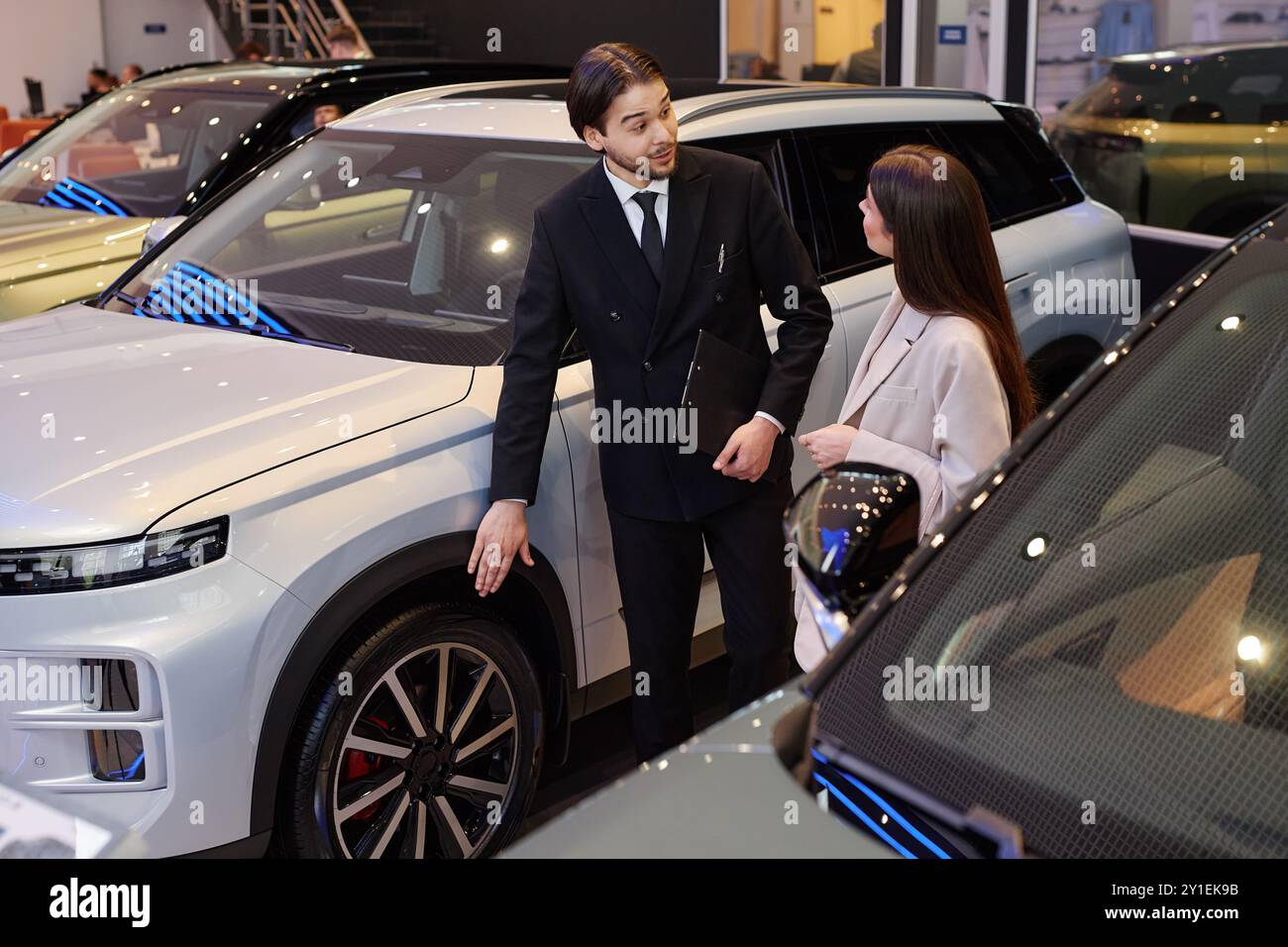 Adult Central Asian male auto dealer telling female customer about car ...