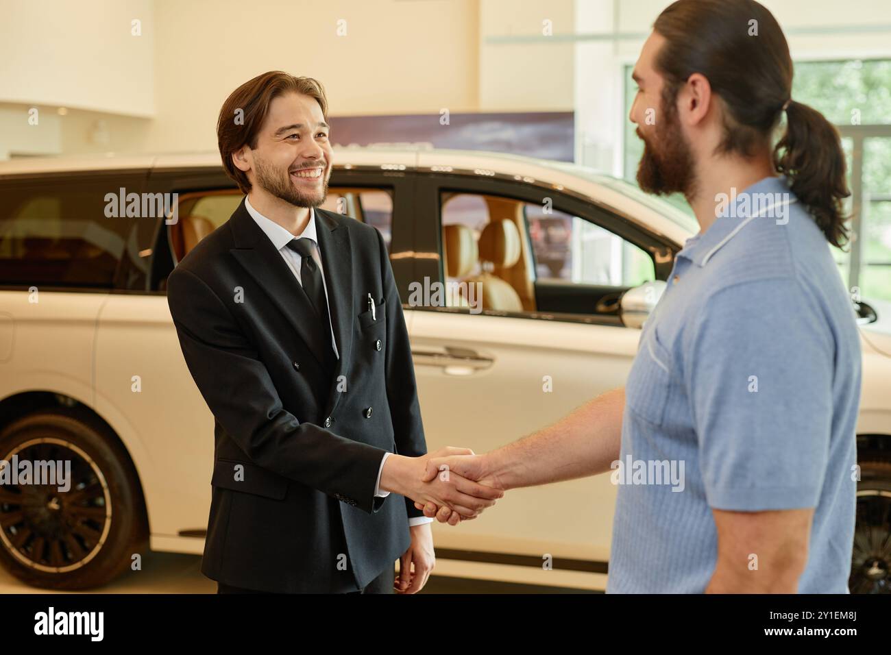 Medium shot of smiling Central Asian male auto dealer shaking hands ...