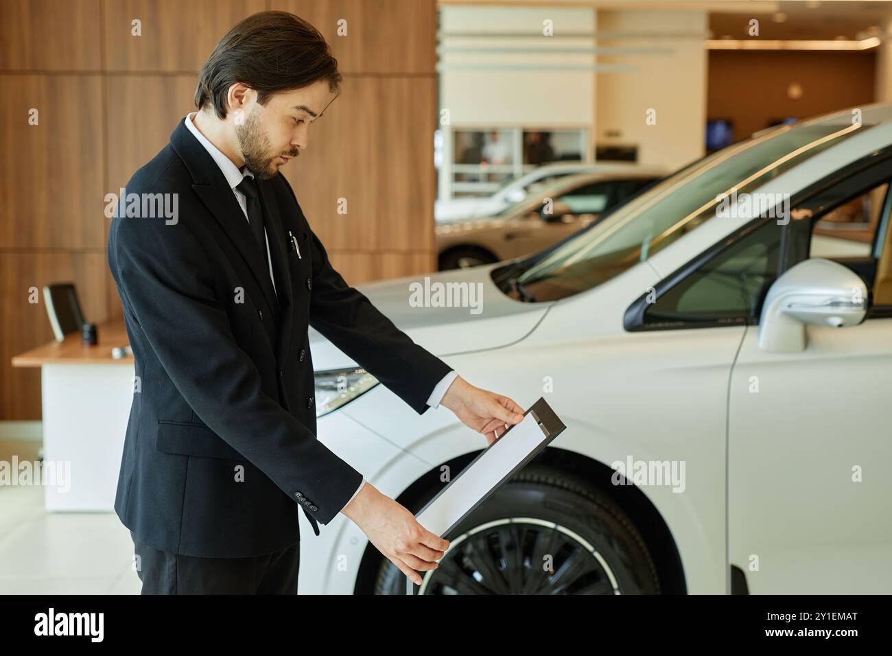 Side view of Central Asian male auto dealer in black suit thoroughly ...