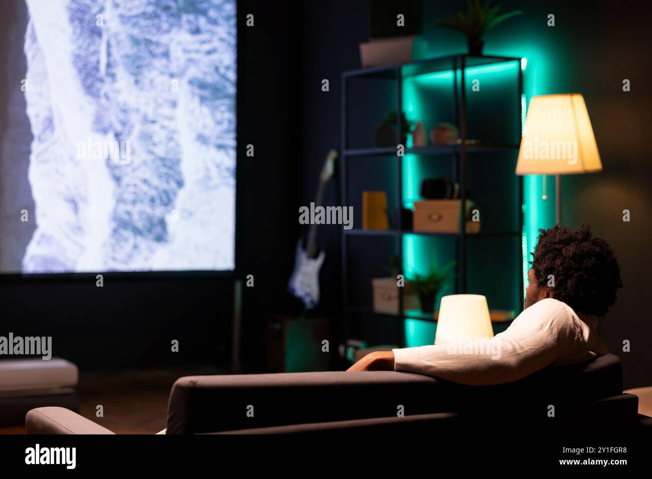 African american man laid up on couch watching nature documentary with ...