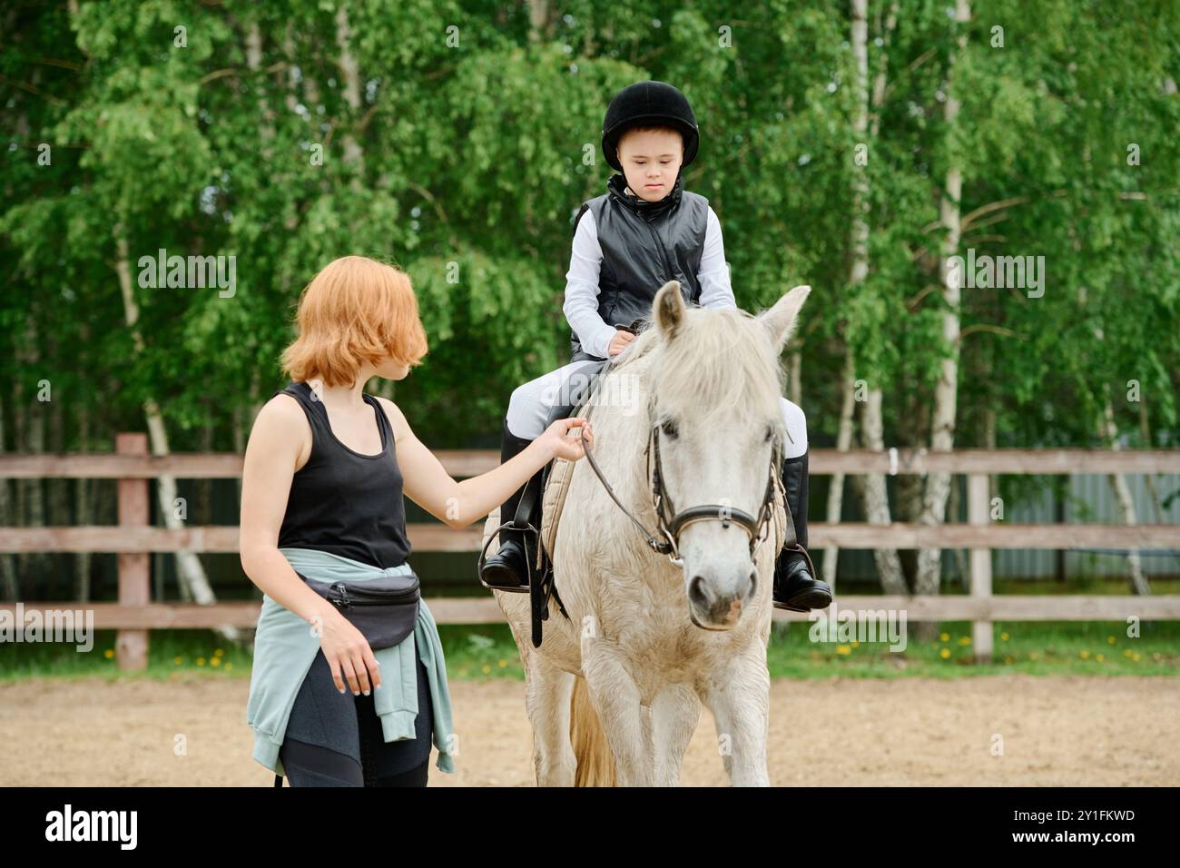 Trainer guiding child during horse riding lesson, with focus on child's ...
