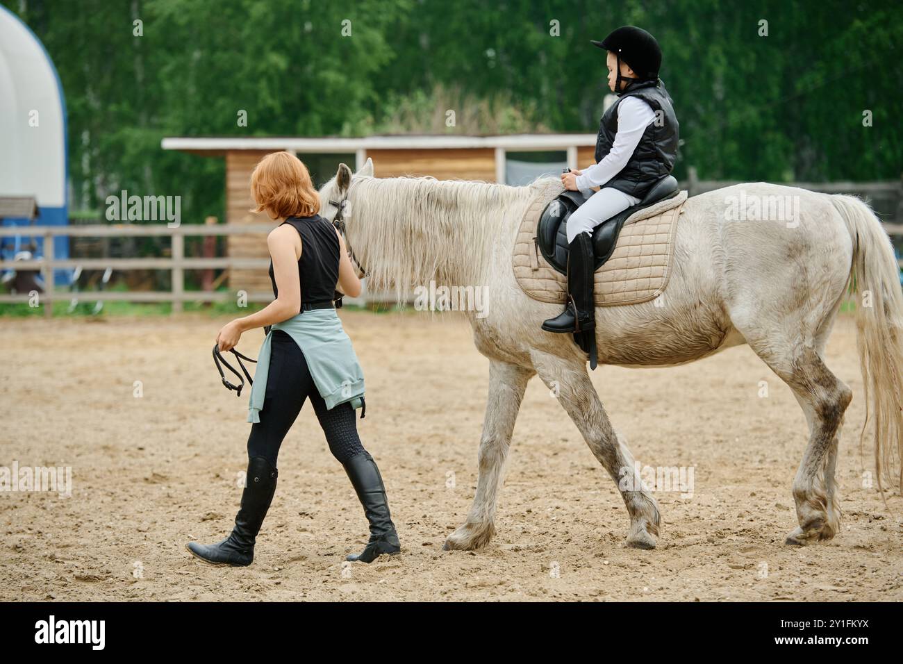 Child learning horseback riding under guidance of adult trainer in ...