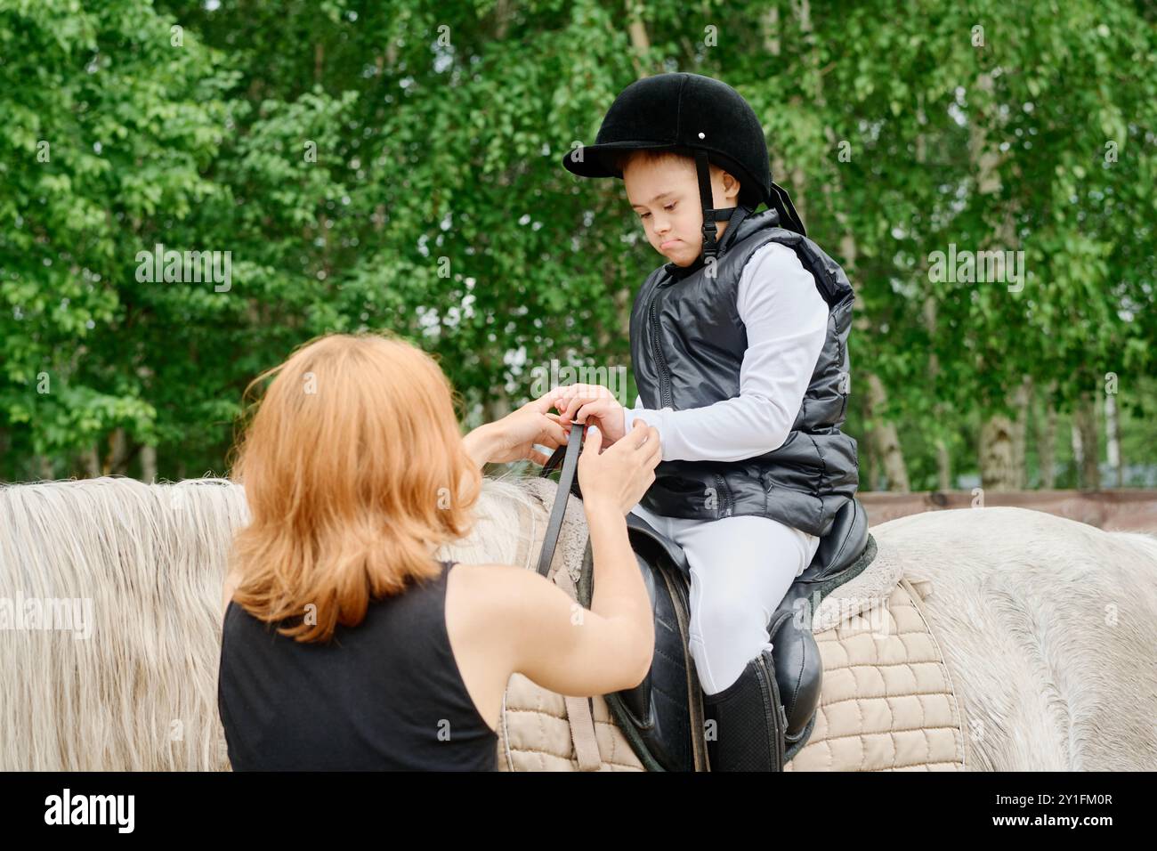 Boy riding horse while wearing helmet and receiving assistance from ...
