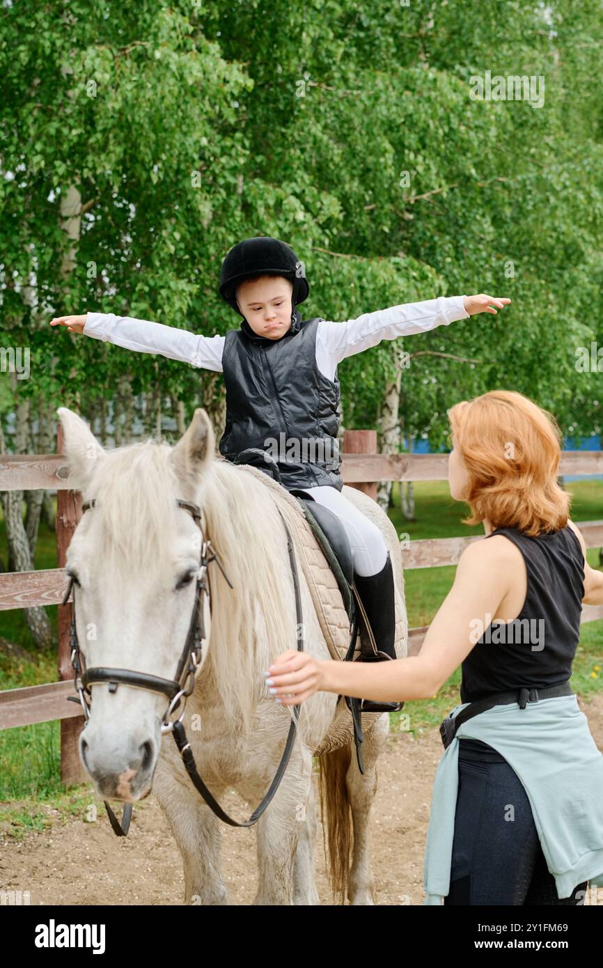 Child practicing horseback riding with an instructor in green forest ...