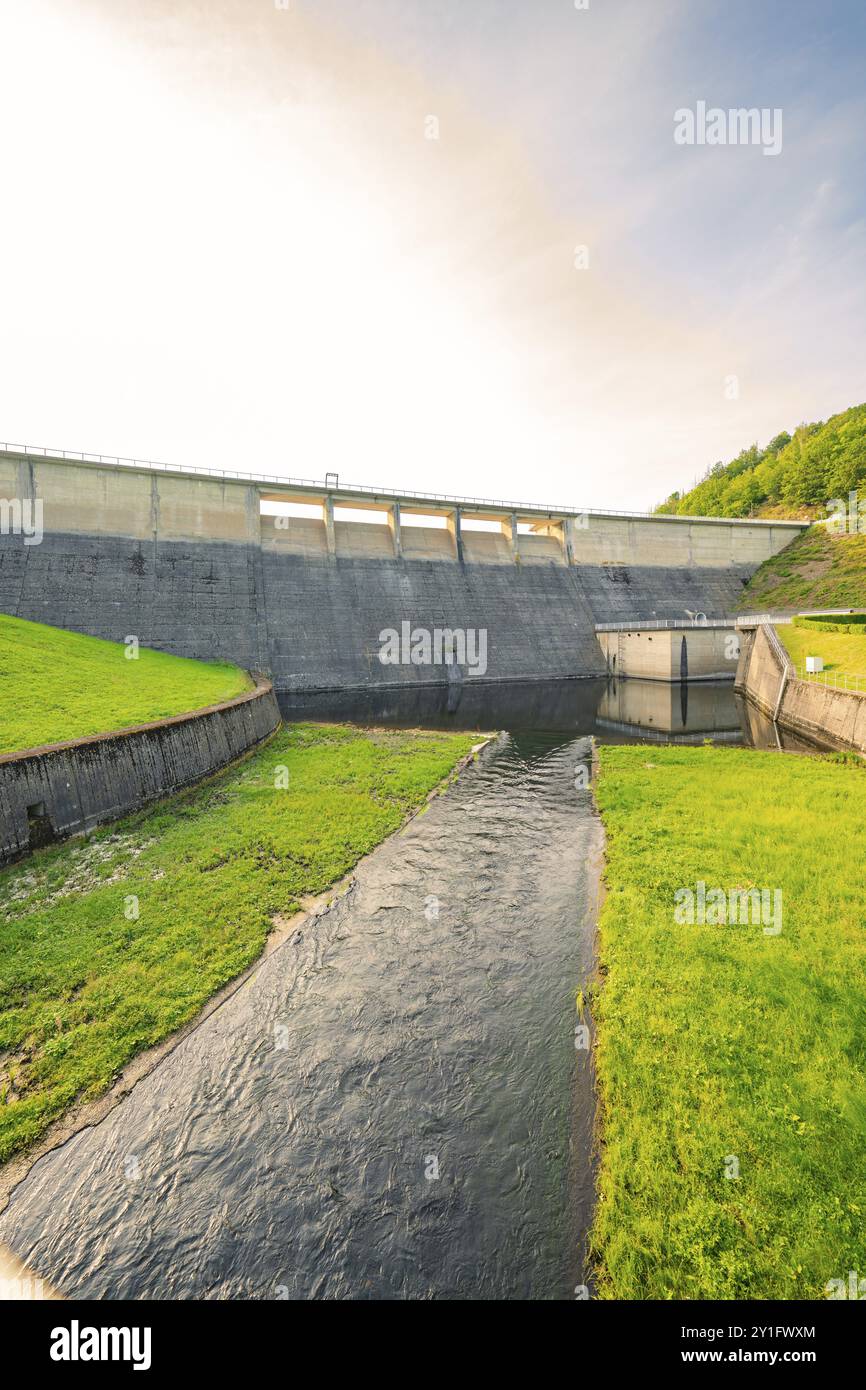 A river flowing under a large concrete dam, surrounded by grass and ...