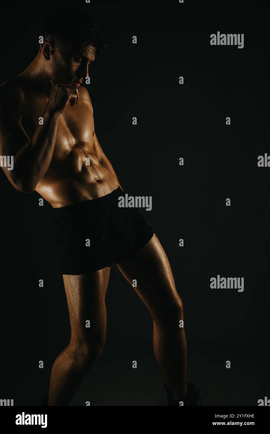 Fit man showing toned abs in dark studio lighting showcasing fitness ...