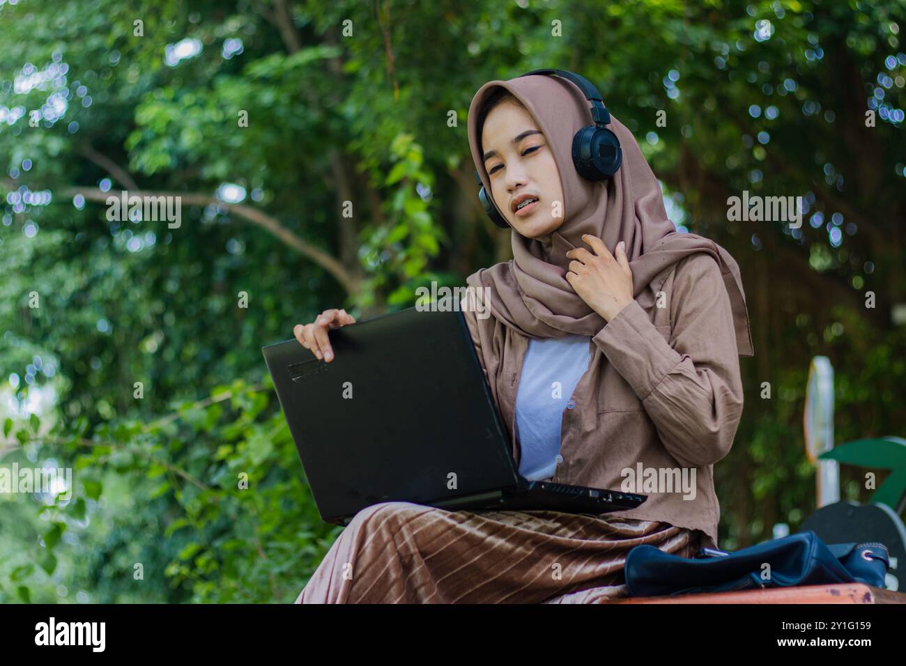gesture indonesia hijab woman suffering from pain in throat while sitting in outdoor park ...