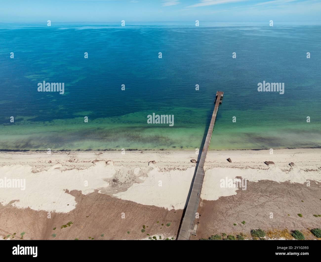 Aerial view of a long narrow jetty out overa white sand beach and the ...