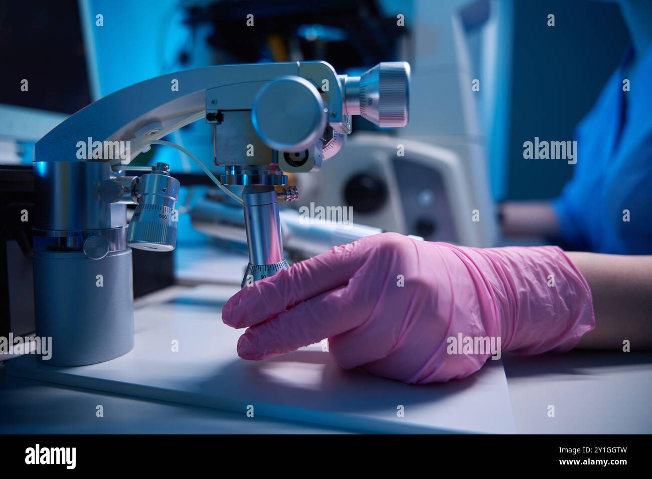 Gloved hand adjusting a micromanipulator under a microscope in ...