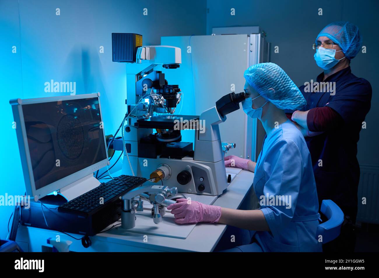 Two lab technicians working with a microscope and computer in a ...