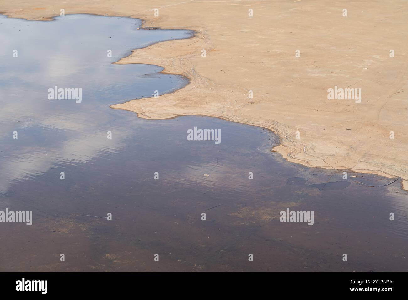 A close-up view of a shallow water body reflecting the sky, with sandy ...