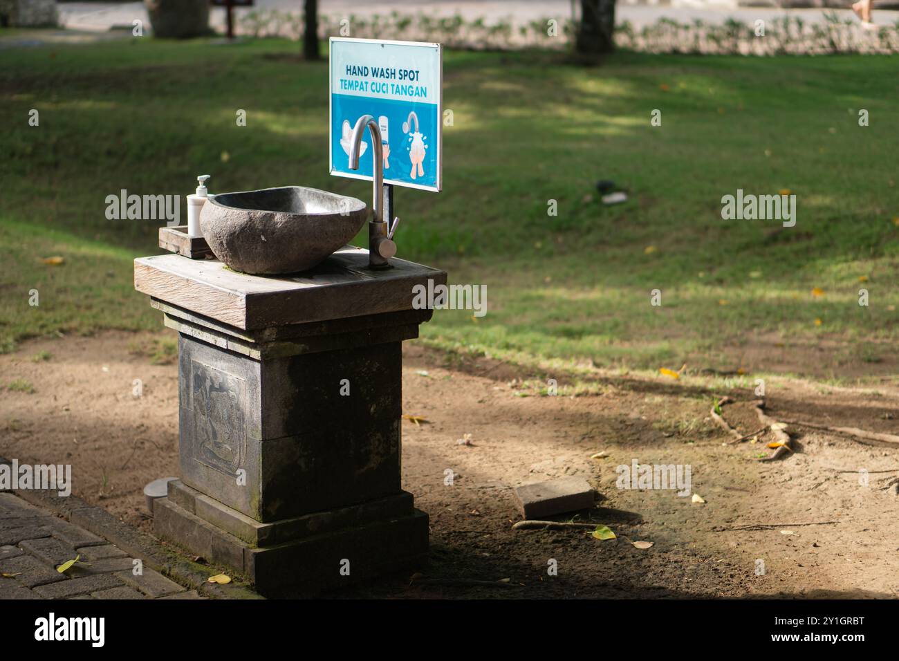 A hand wash station in a park, featuring a stone basin and a faucet. A ...