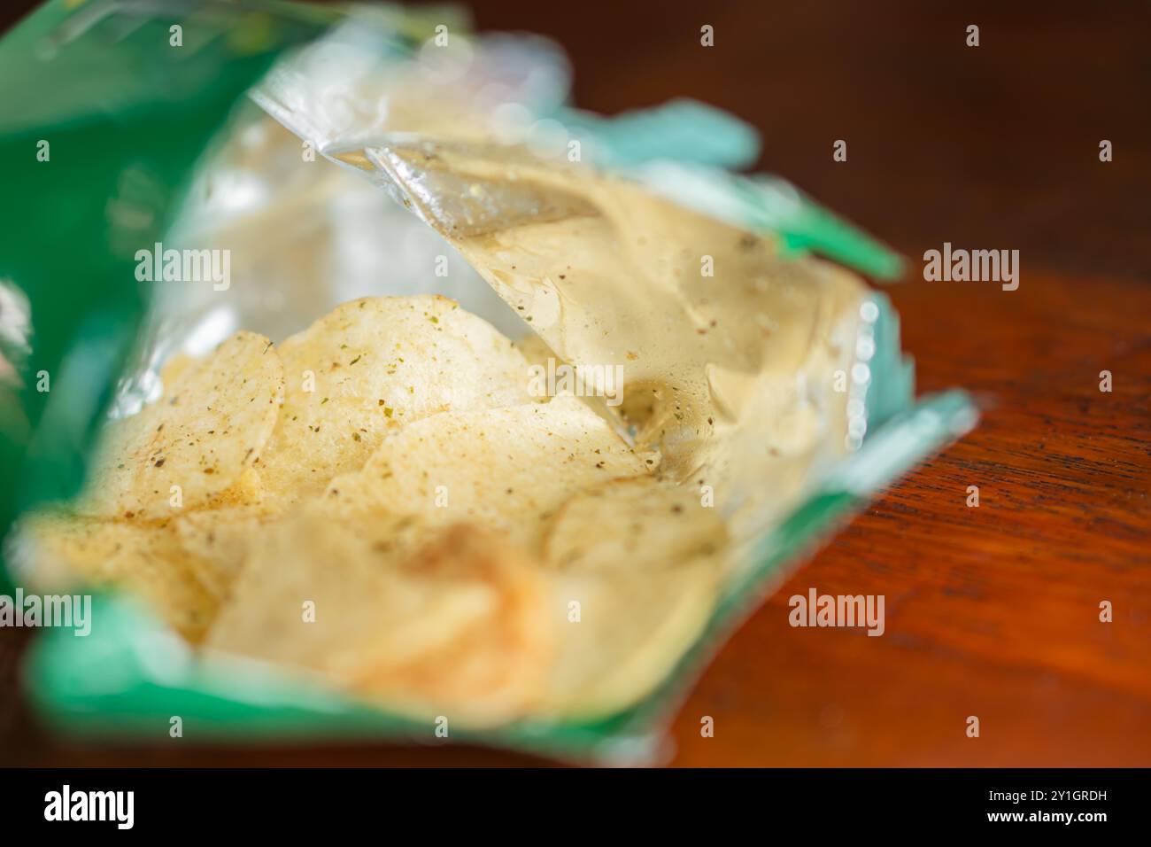 An open bag of potato chips with some chips spilling out onto a wooden ...