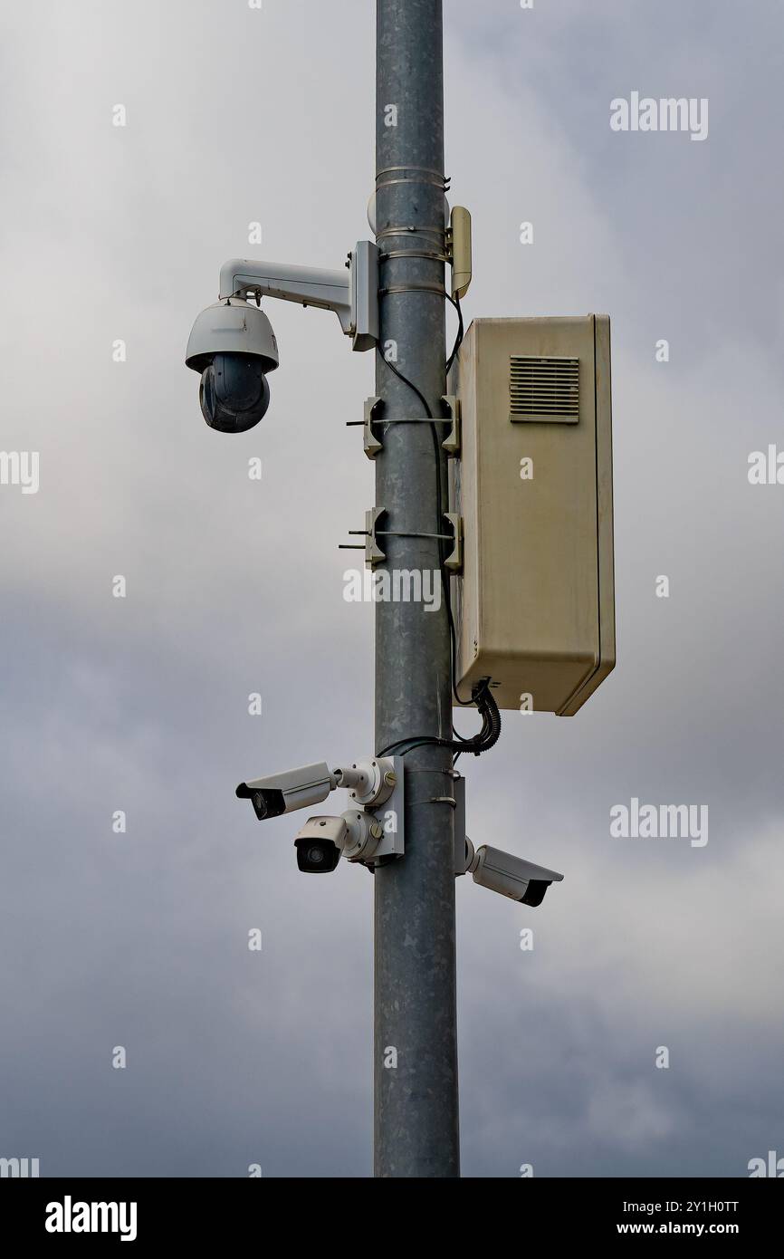 Four security cameras connected to a metal post, with an overcast sky ...