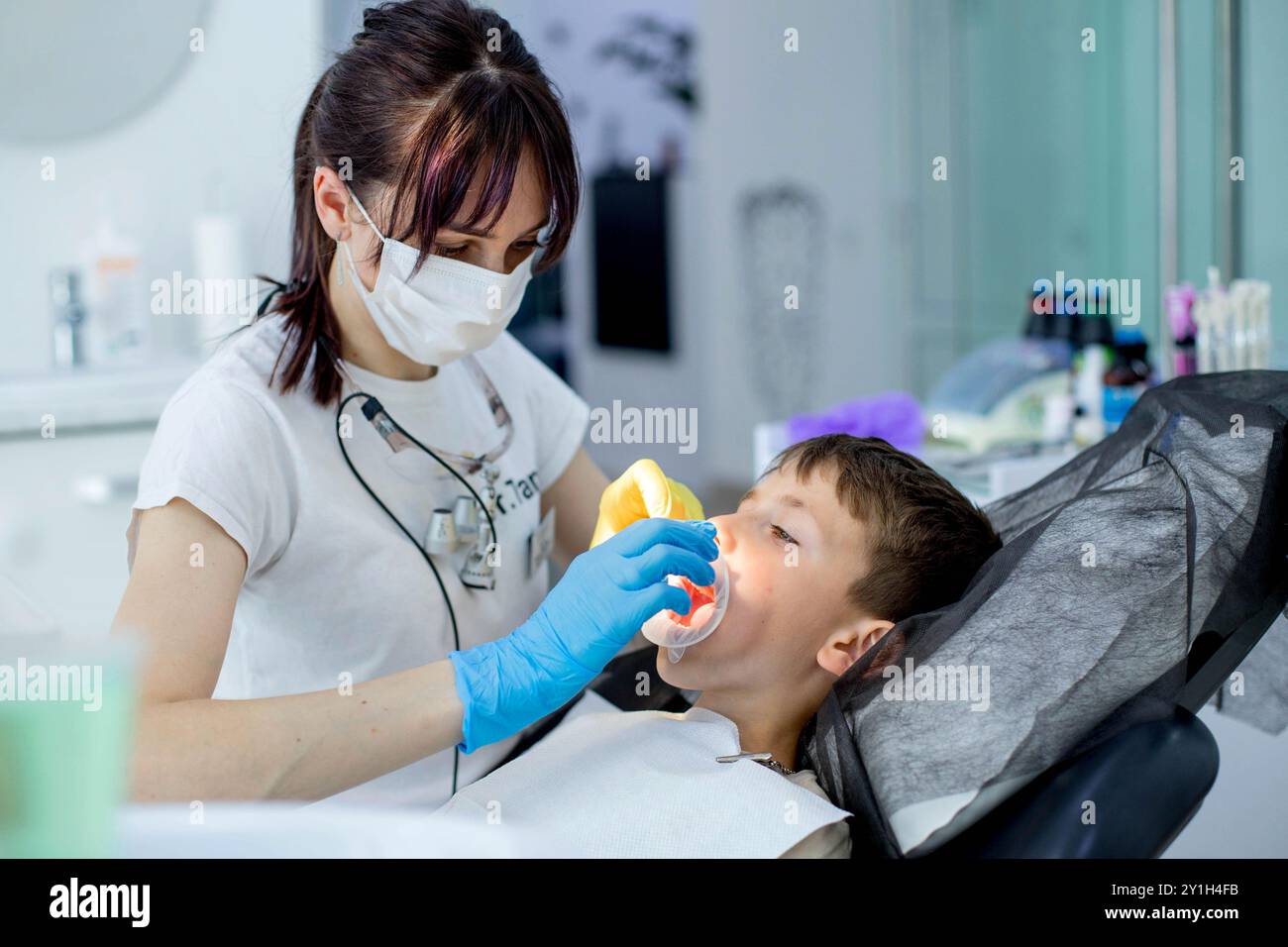 Paediatric dentist putting a cheek retractor on child patient before ...