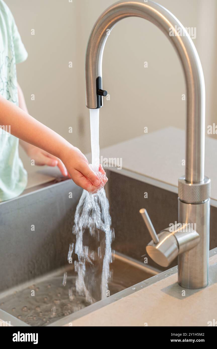 Little kid washing his hands and playing with the water in the kitchen ...