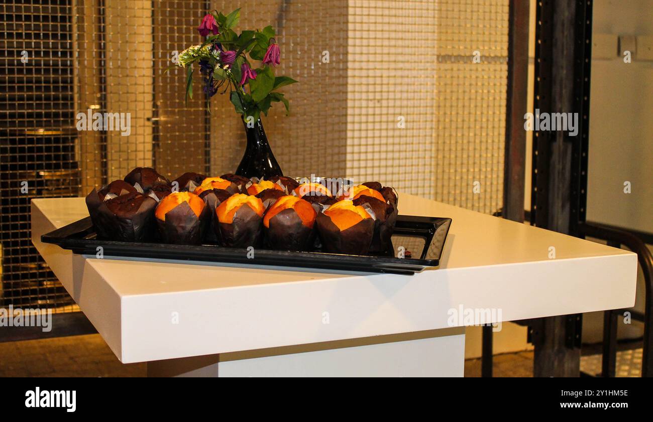 A modern table displaying a tray of assorted muffins, including ...