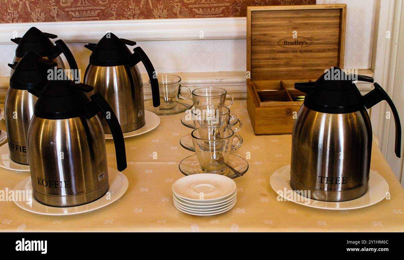 A table set with several stainless steel coffee and tea pots labeled ...