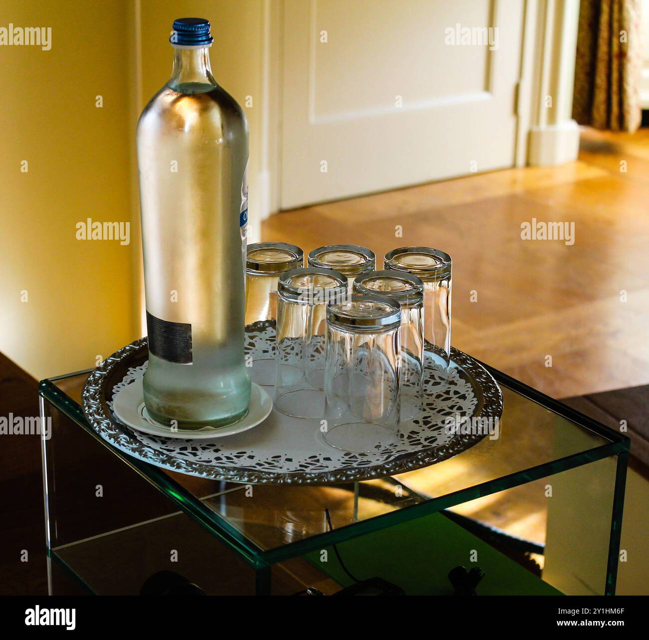 A glass bottle of water placed on a decorative tray with six empty ...