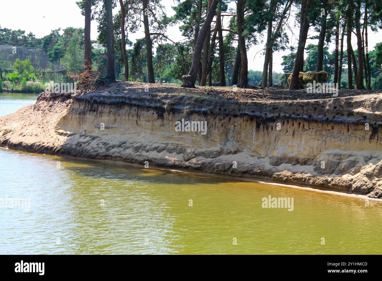 A serene lakeside view featuring a sandy bank with exposed layers of ...