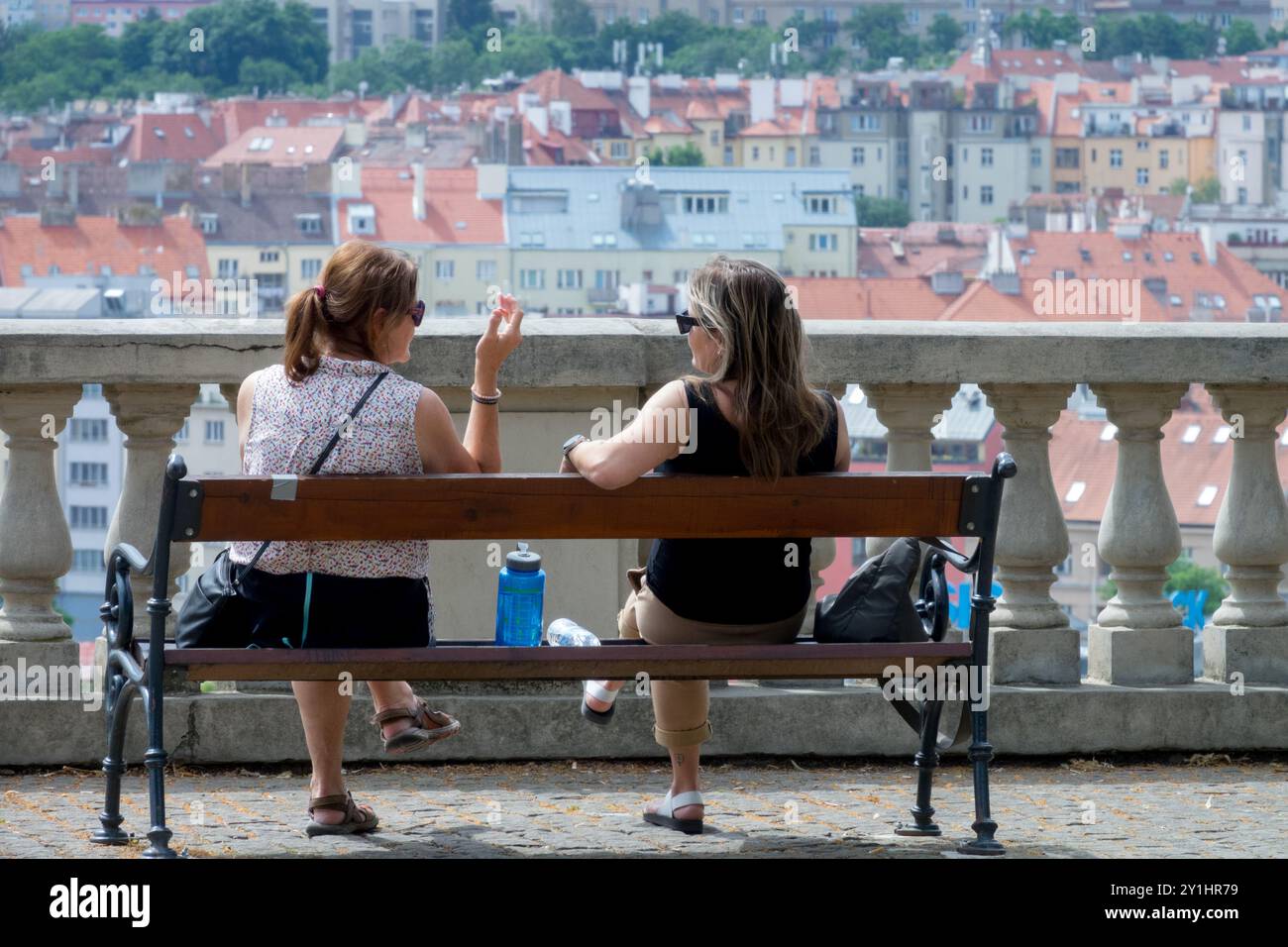 Two women sitting on a bench talking while enjoying a city view with ...